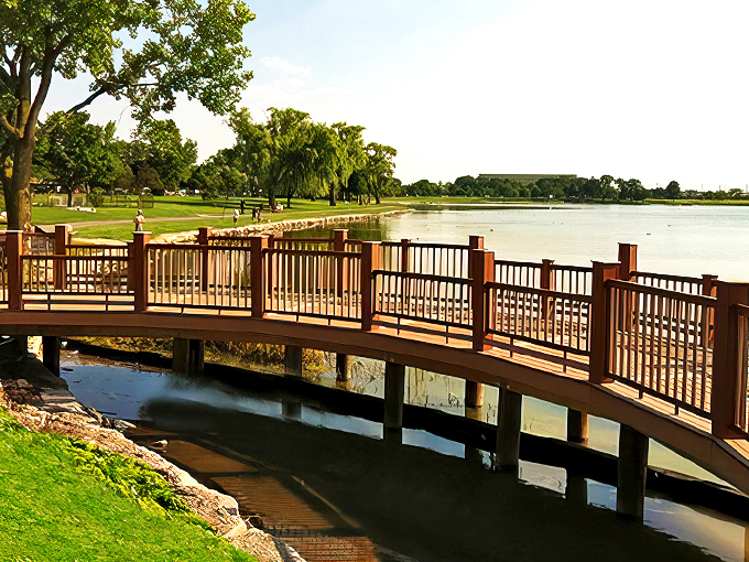 A gracefully curved wooden bridge spans the water like nature's welcome mat, inviting visitors to explore Lake Park's serene beauty.