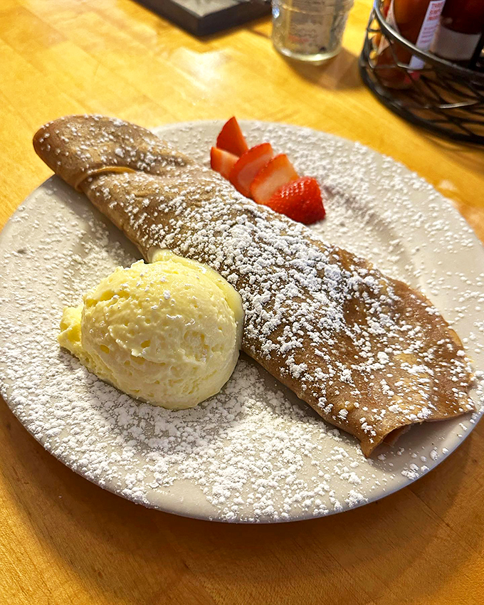 A delicate crepe dressed in powdered sugar, with fresh strawberries adding a pop of color and sweetness. 