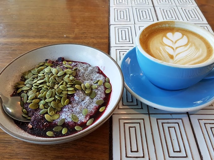 The perfect morning duo: a hearty bowl of berry-topped porridge alongside an expertly crafted latte with leaf art.