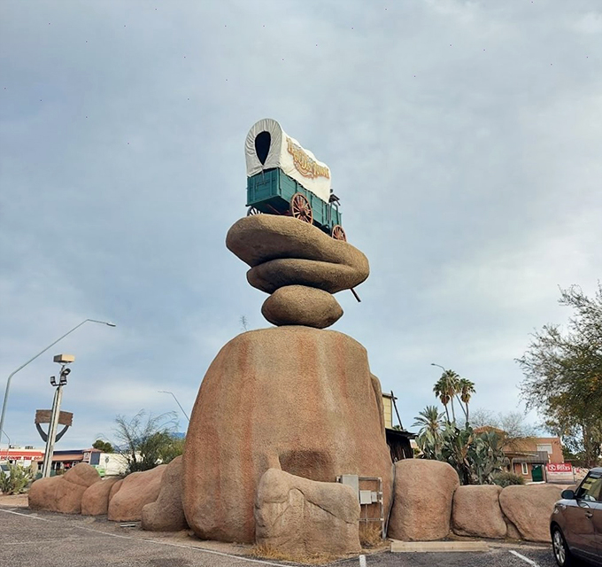 A whimsical rock formation topped with a covered wagon serves as Trail Dust Town's iconic landmark against the Arizona sky.