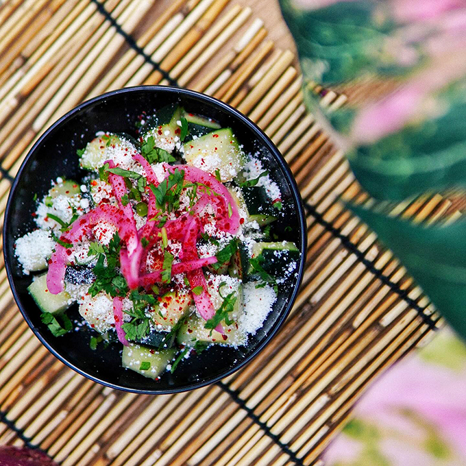 A work of art in black and pink, where cucumbers meet cotija cheese under a shower of chili flakes.