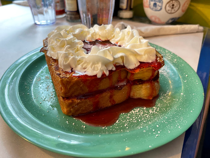 French toast that looks like it graduated from culinary school with honors. Crispy, custardy, and crowned with a cloud of whipped cream.