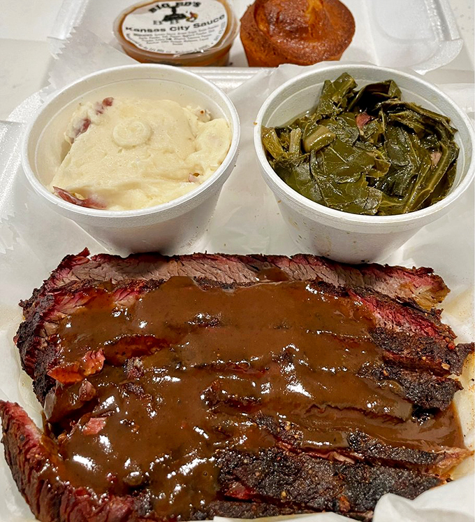 Sliced brisket getting cozy with house sauce, while collard greens and potato salad round out the perfect plate.