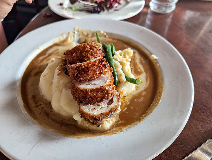 Crispy breaded chicken rests on a cloud of mashed potatoes, surrounded by a sauce that would make Julia Child proud.