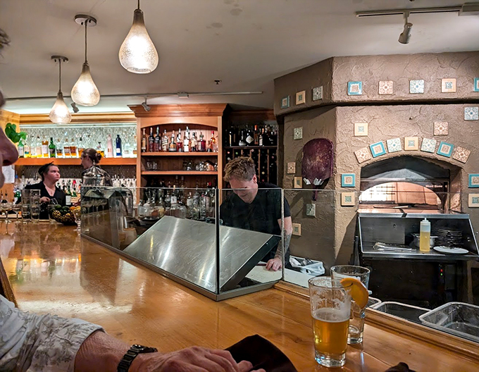 Teardrop lights illuminate the copper bar top, while decorative tiles frame the pizza oven like a culinary art installation.