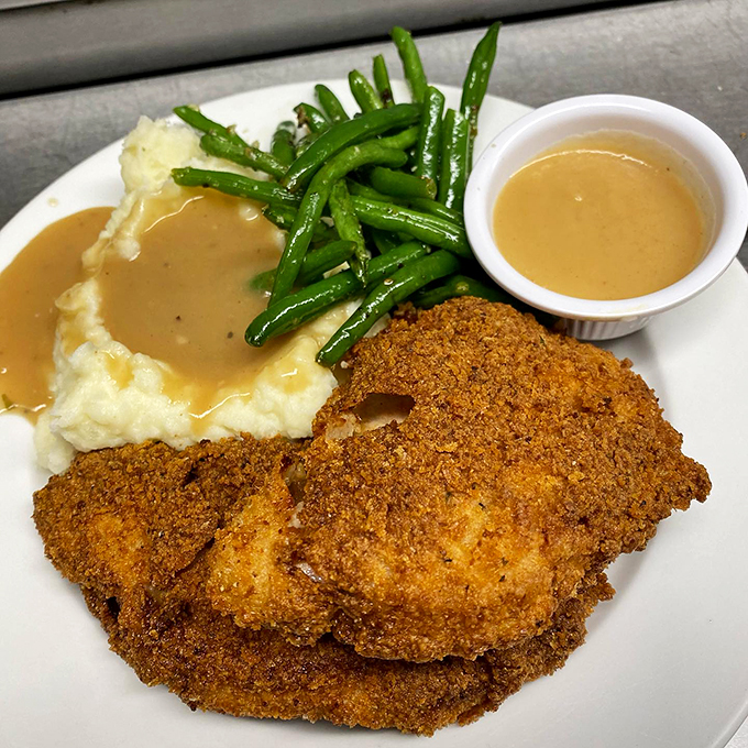 A golden-crusted pork chop served with green beans and mashed potatoes - comfort food elevated to an art form.