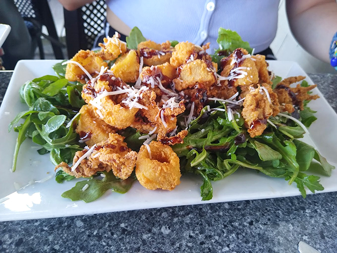 Crispy calamari perches atop fresh greens like a golden crown, drizzled with a sauce that means business.