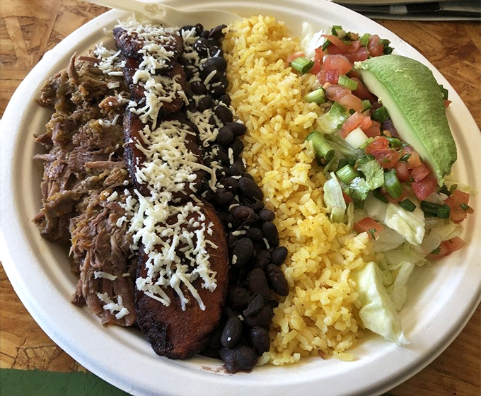 A colorful fiesta on a plate: tender carnitas, yellow rice, and black beans, with fresh pico and avocado adding the final flourish.