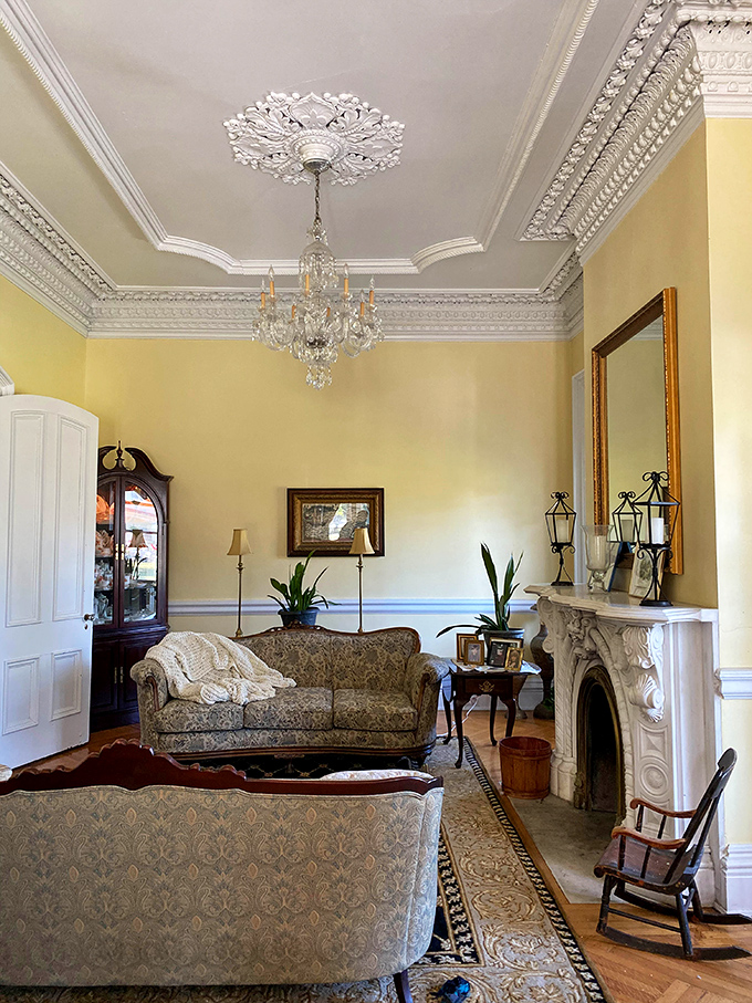 Sunlight streams through tall windows into the double parlor, where crystal chandeliers and ornate moldings whisper tales of Victorian elegance.