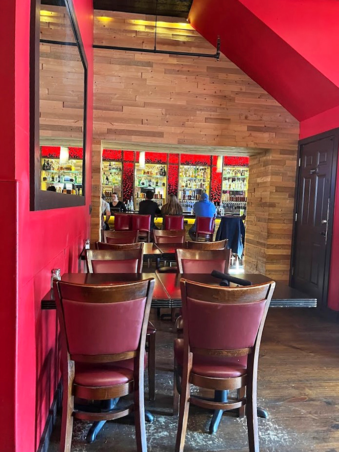 Rich burgundy chairs and wood-paneled walls create an intimate dining space that feels both modern and cozy. The bar beckons in the background.