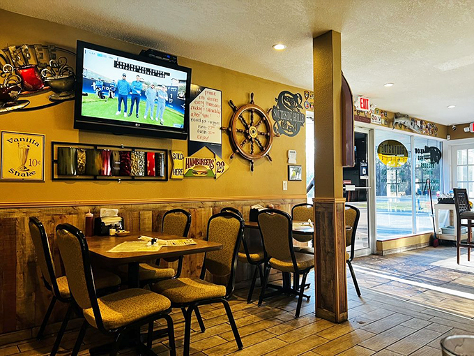 Rustic wood paneling meets cozy seating in this warm dining space, where a ship's wheel adds nautical charm to the walls.