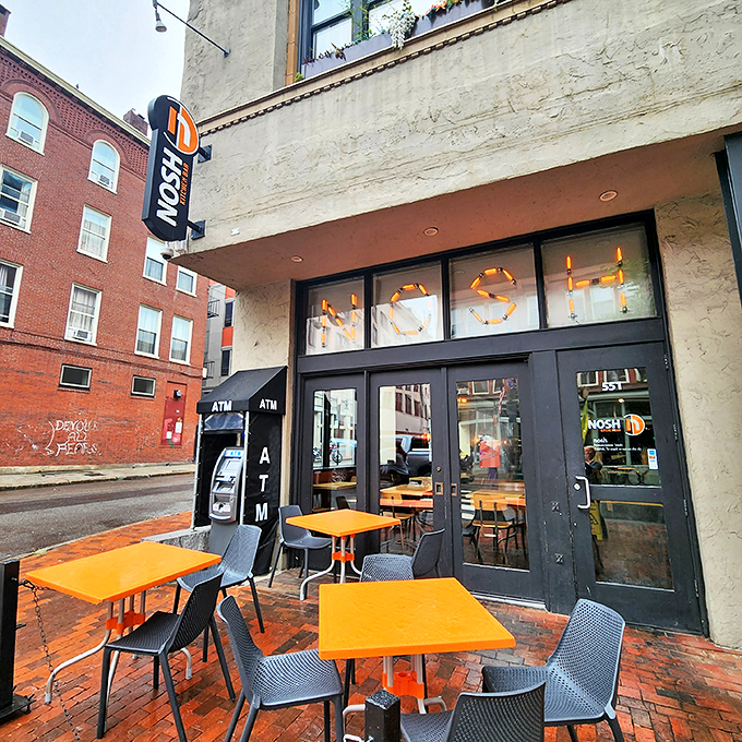 Nosh Kitchen Bar: Where industrial chic meets comfort food paradise. Those orange tables? Like beacons guiding you to burger bliss.