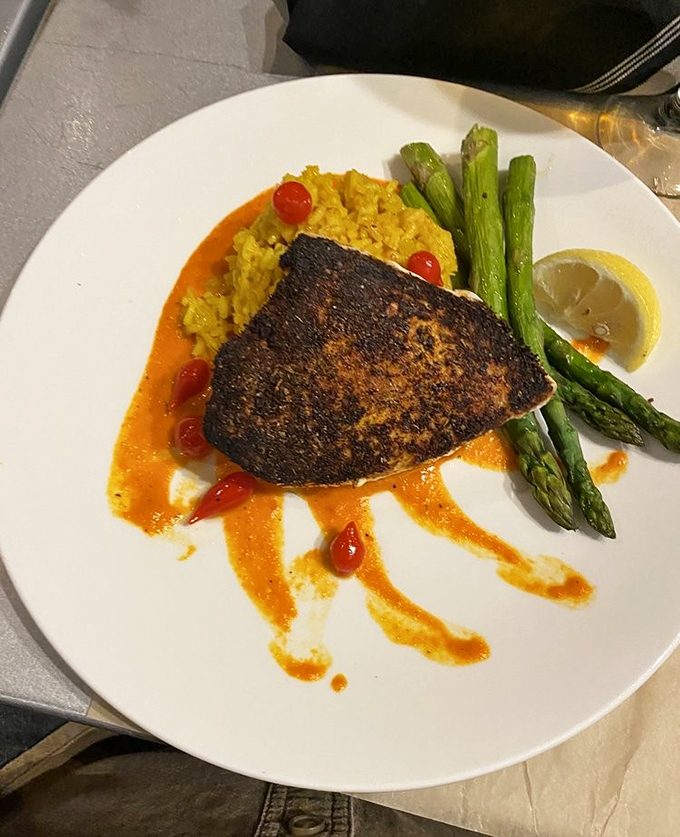 A perfectly blackened swordfish rests on saffron rice like modern art, with asparagus standing at attention and cherry tomatoes adding playful pops of color.