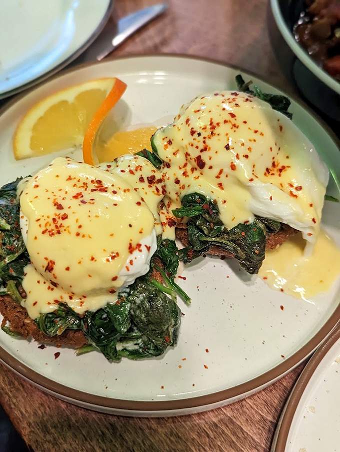 A masterpiece of perfectly poached eggs draped in hollandaise, perched atop a bed of vibrant saut&eacute;ed greens.