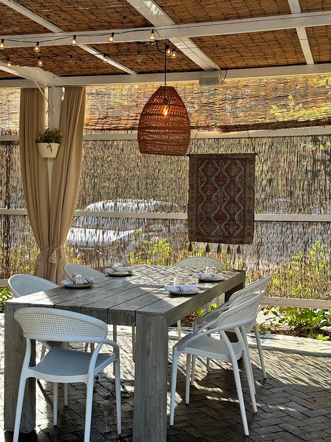 The outdoor dining area feels like a secret garden, complete with woven screens and pendant lights casting a warm glow. Photo credit: Olivia Petrella
