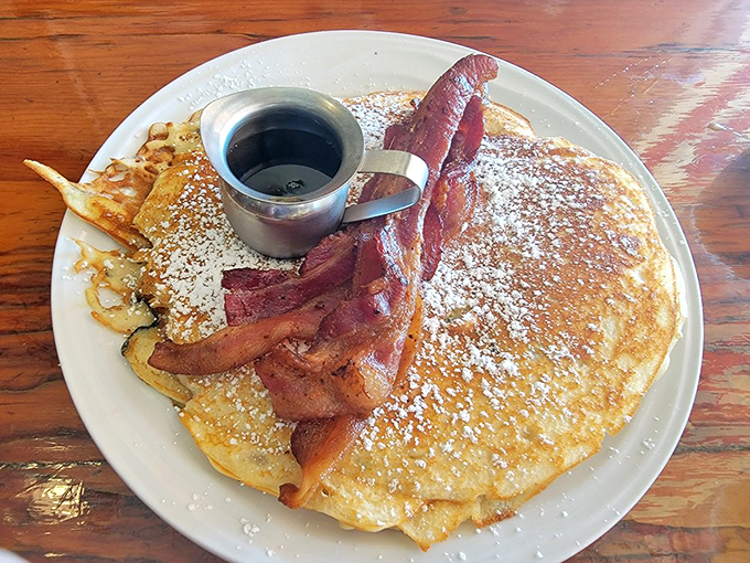 Golden-brown perfection meets maple syrup heaven in this plate-sized pancake, with bacon standing guard like delicious sentinels.