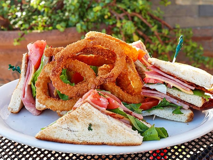 This isn't just a club sandwich - it's a towering masterpiece of fresh ingredients, crowned with perfectly crispy onion rings. Photo credit: 5th Avenue Cafe