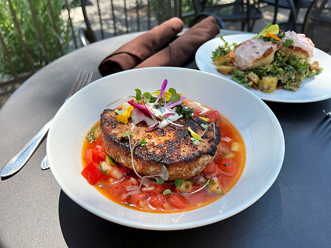 A perfectly seared crab cake rests like an island in a sea of vibrant tomato broth, crowned with edible flowers.