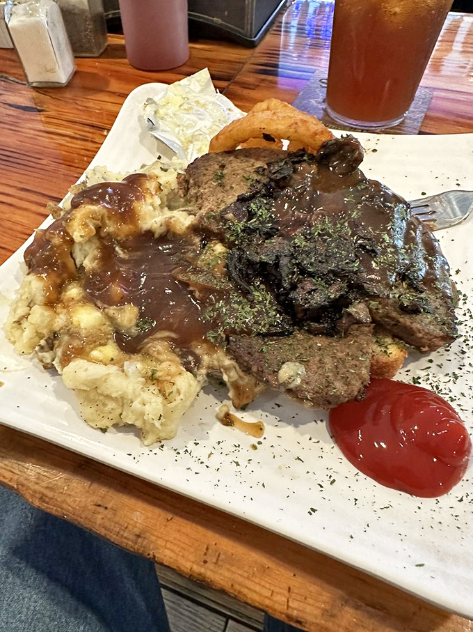 A generous portion of meatloaf swimming in rich brown gravy, paired with cloud-like mashed potatoes and colorful vegetables.
