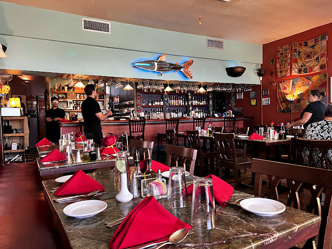 A bustling dining room where red napkins pop against dark wood tables, creating an atmosphere of casual elegance.