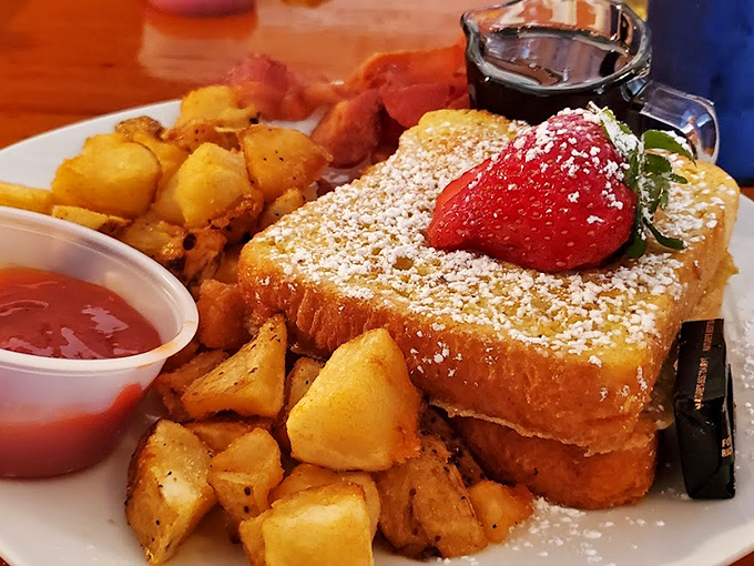 A breakfast masterpiece: French toast dusted with powdered sugar, crowned with fresh strawberries and surrounded by golden home fries.