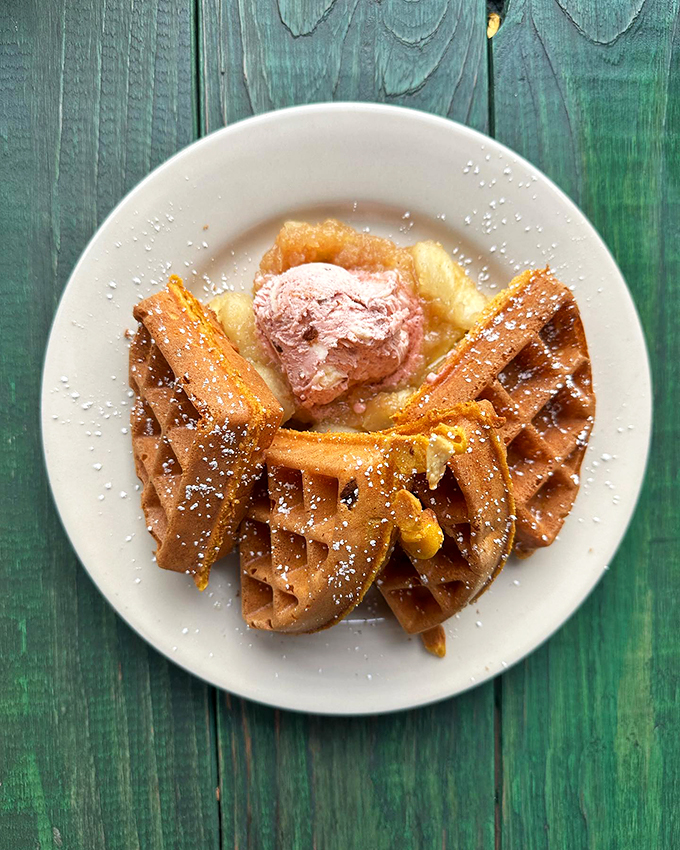 A Belgian waffle that's living its best life, crowned with a scoop of ice cream and dusted with powdered sugar.