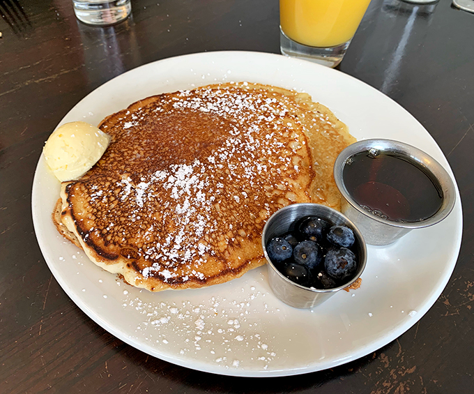 Pancake perfection achieved! Golden discs of joy, dusted with powdered sugar snow, flanked by nature's candy. Breakfast bliss, served on a plate.