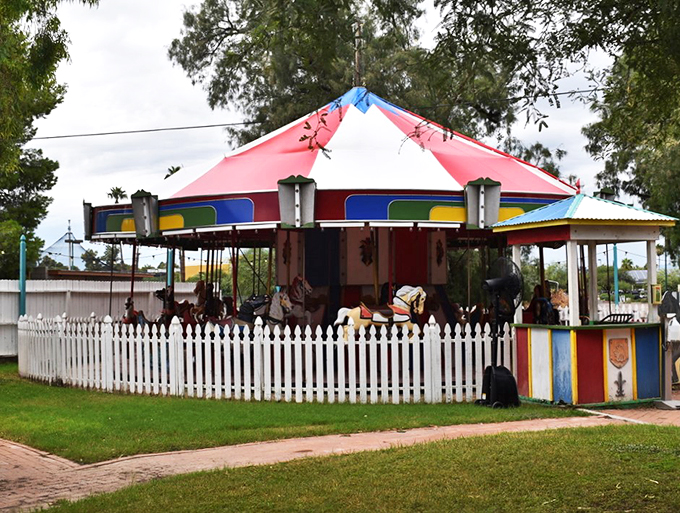 A classic carousel brings smiles to faces young and old, surrounded by a pristine white picket fence under Arizona skies.