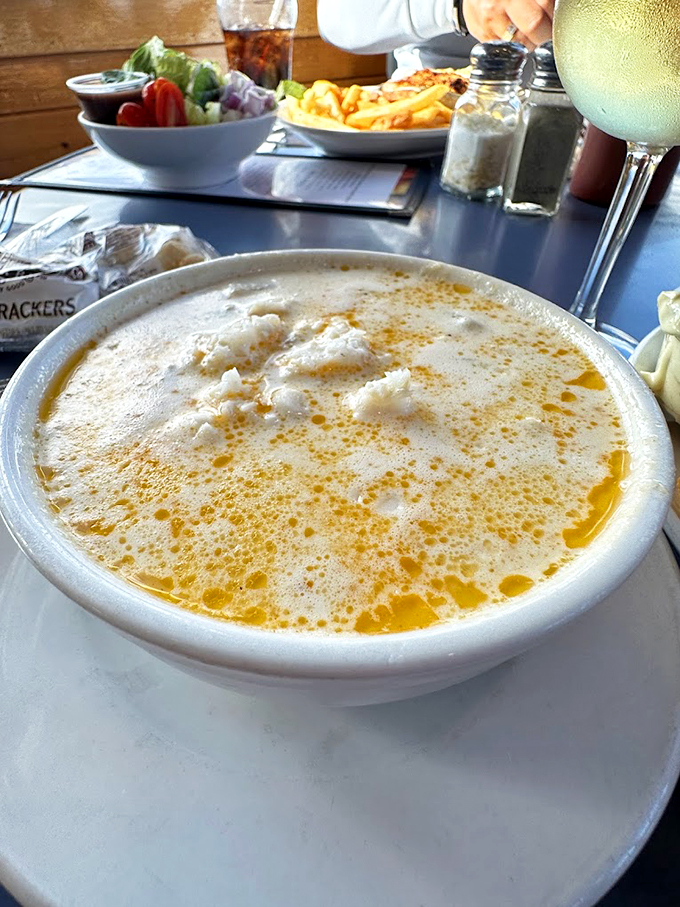 Golden butter swirls dance atop this legendary chowder, promising treasures of tender clams nestled below the surface.