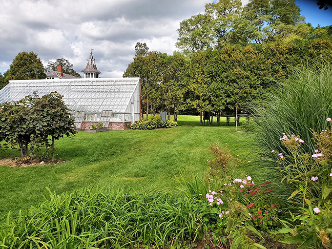 The greenhouse peeks through manicured gardens, where flowers dance in formation like nature's own Broadway show.