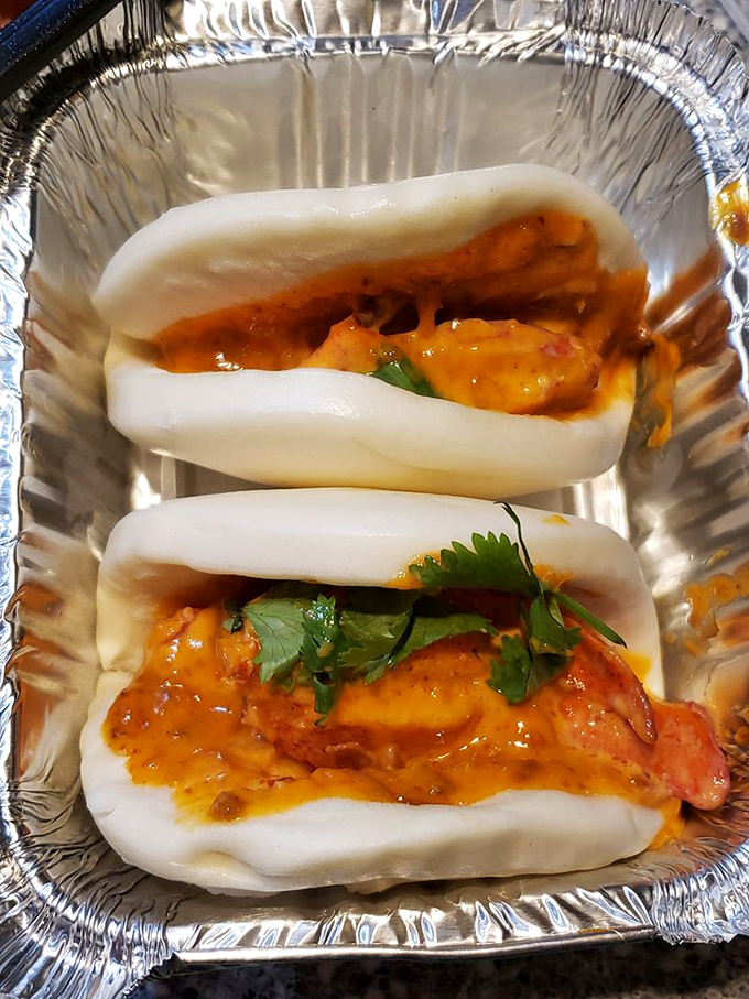 Pillowy steamed bao cradles succulent meat in a warm embrace, topped with a splash of vibrant sauce.