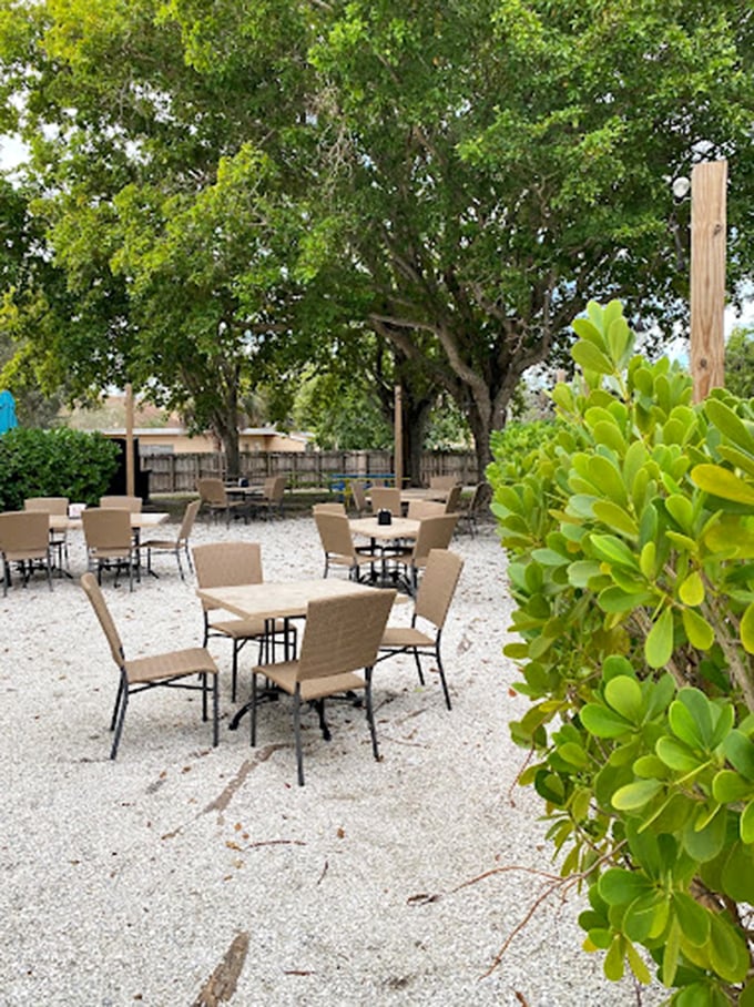 A tranquil garden oasis awaits, where towering trees provide natural shade over casual seating perfect for Naples' beautiful weather.