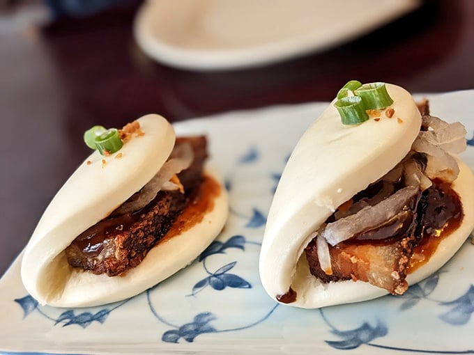 Tender pork belly nestled in cloud-like bao buns, garnished with fresh scallions for the perfect bite.