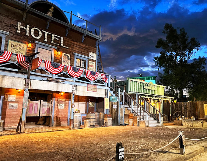 As evening falls, the old hotel comes alive with warm lamplight and patriotic bunting, creating an atmospheric Old West scene.