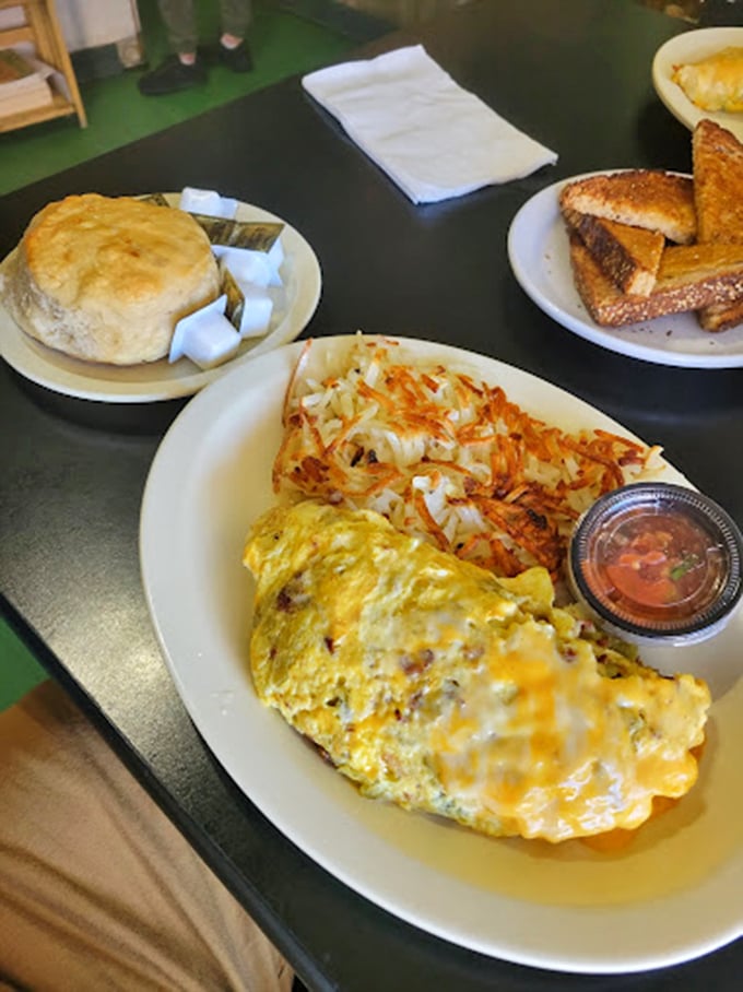 A perfectly folded omelet shares the plate with crispy hash browns and a fluffy biscuit - breakfast nirvana achieved.