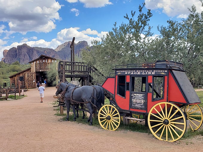 Step back in time at the Superstition Mountain Museum, where a vibrant red stagecoach and rustic barn transport visitors to the Wild West, set against Arizona's rugged mountain backdrop.