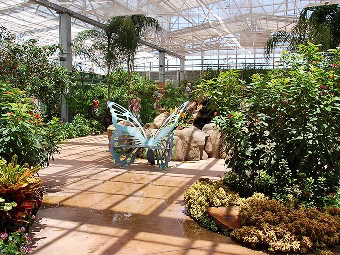 Lush tropical paradise thrives under glass roof, with vibrant plants and a whimsical butterfly sculpture creating a serene oasis.