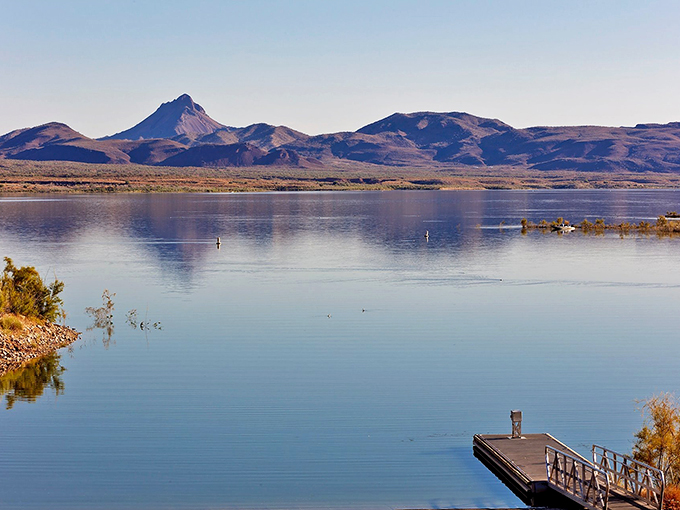 Tranquil waters of Alamo Lake mirror the rugged beauty of Arizona's desert mountains, with a lone dock inviting adventure seekers to dive into nature's serenity.