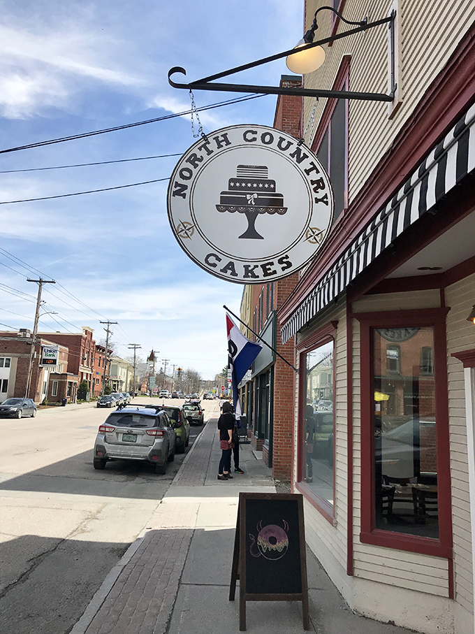 The iconic North Country Cakes sign swings like a beacon of hope for donut lovers on Morrisville's main street. Small-town charm meets serious baking.