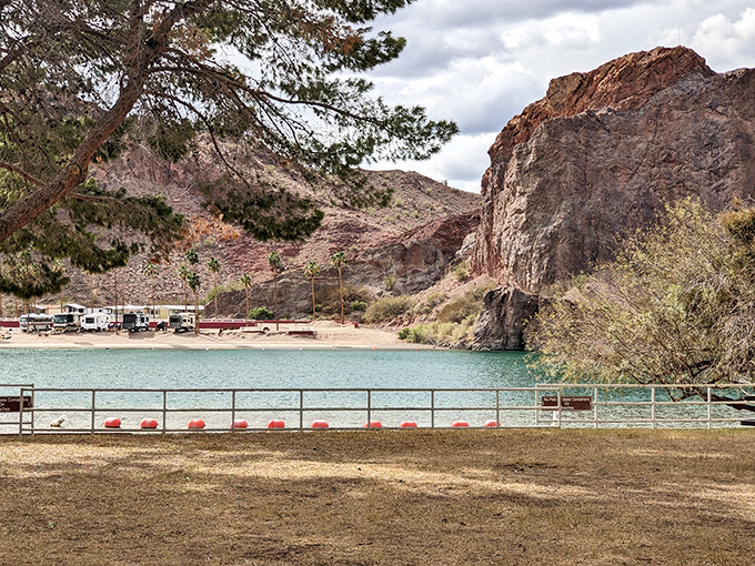 Nature's amphitheater: Rugged cliffs embrace a tranquil lake, while RVs nestle at the water's edge, creating a perfect harmony of wild beauty and cozy camping at Buckskin Mountain State Park.