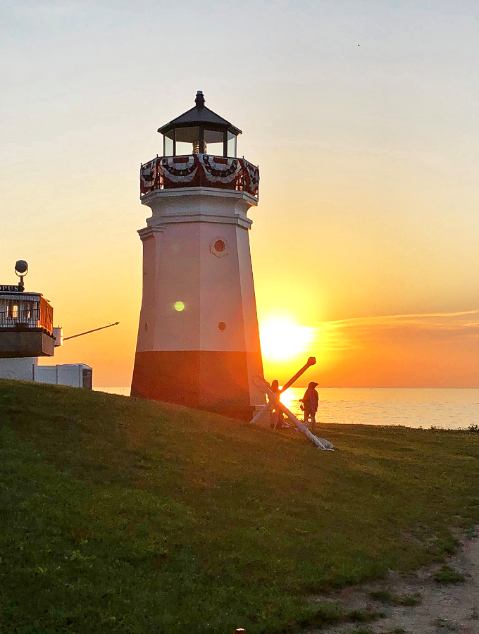 "Sunset paints the sky in hues that'd make Bob Ross proud. Our lighthouse, basking in the glow, is having its own 'happy little accident' moment."