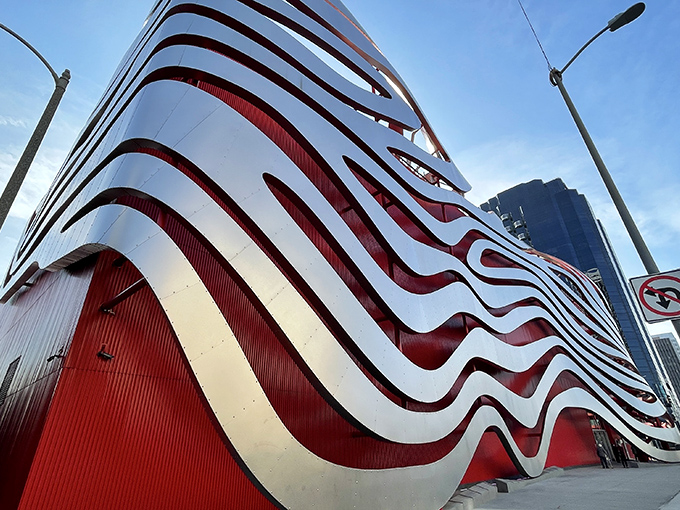 Buckle up, car enthusiasts! This architectural marvel looks like a giant decided to gift-wrap the Petersen Automotive Museum with ribbons of stainless steel and red aluminum.
