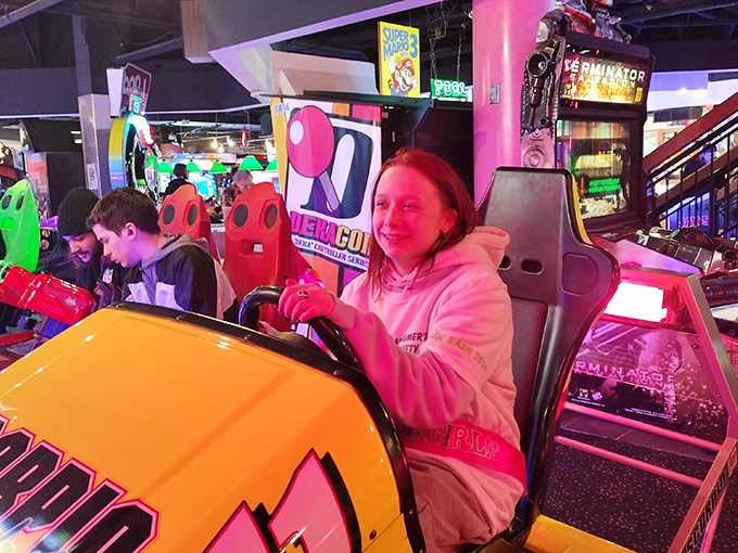 Racing to victory or just enjoying the ride? Either way, this gamer's grin is brighter than the neon signs around her.