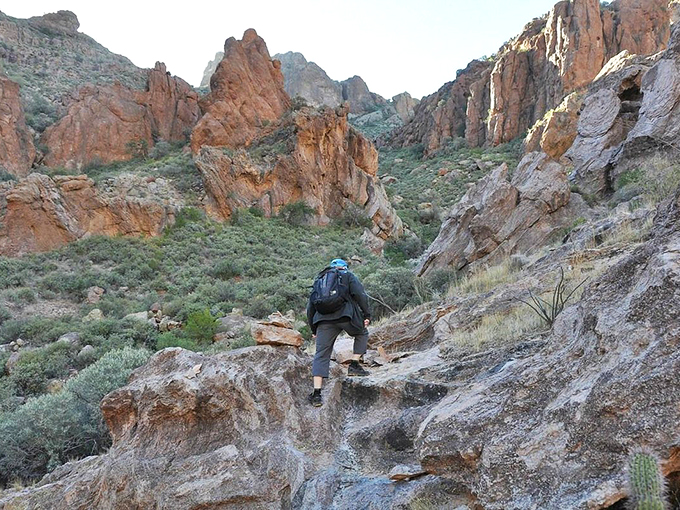 A lone hiker navigates rugged terrain amidst towering rock formations in the Sonoran Desert near Ajo. Nature's grandeur dwarfs human presence, offering a thrilling adventure for outdoor enthusiasts.