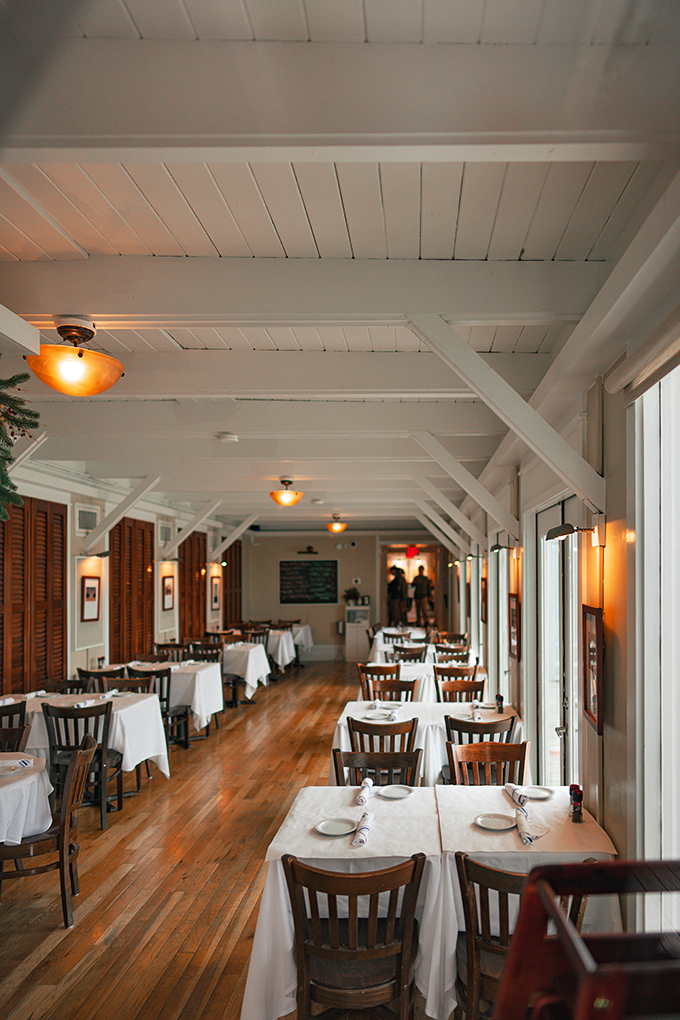 Step into a coastal dream! This dining room's warm wood and soft lighting create an atmosphere cozier than your favorite cardigan on a breezy beach night.