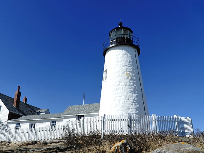 Crisp white picket fences and weathered shingles - this lighthouse looks like it stepped right out of a Norman Rockwell painting.