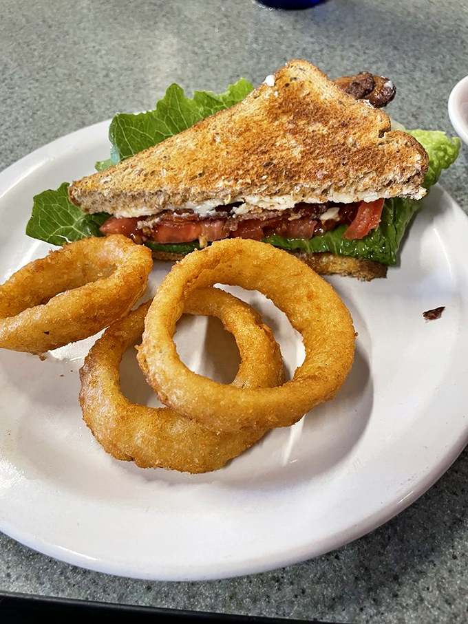 The BLT: Breakfast, Lunch, or Triumph? This sandwich, flanked by golden onion rings, is ready to take on any mealtime challenge.