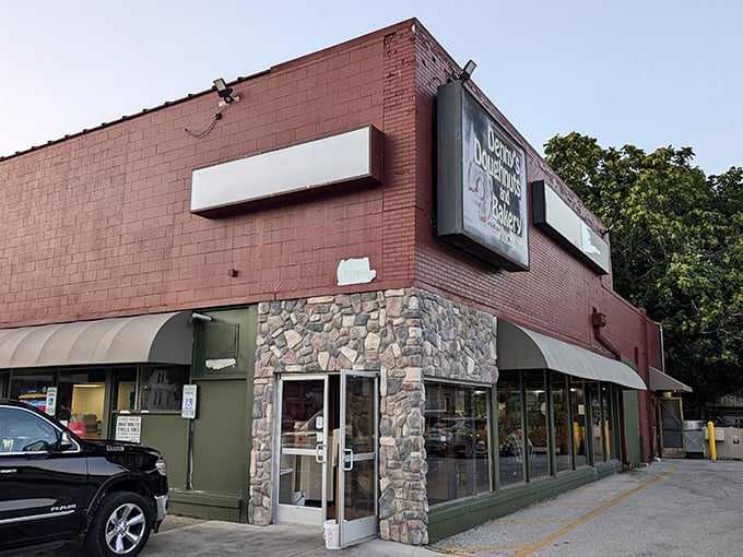Welcome to carb heaven! Denny's Doughnuts and Bakery stands like a beacon of sugary hope on the corner, its red brick and yellow awnings promising sweet salvation.