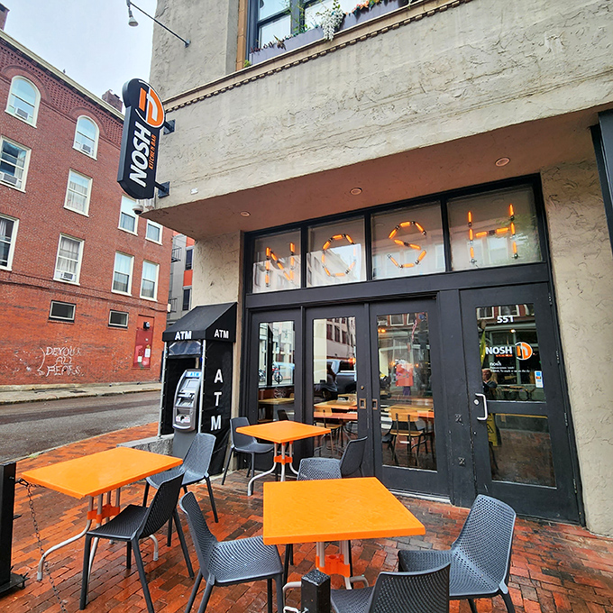 Welcome to burger paradise! Nosh's vibrant exterior promises a feast for the senses, with its eye-catching orange tables inviting you to sit and savor.