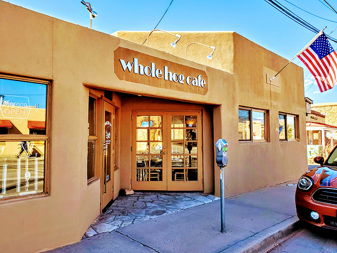 Welcome to flavor town! Whole Hog Café's adobe exterior is like a siren song for barbecue lovers, with that American flag waving you in for a taste of smoky paradise.